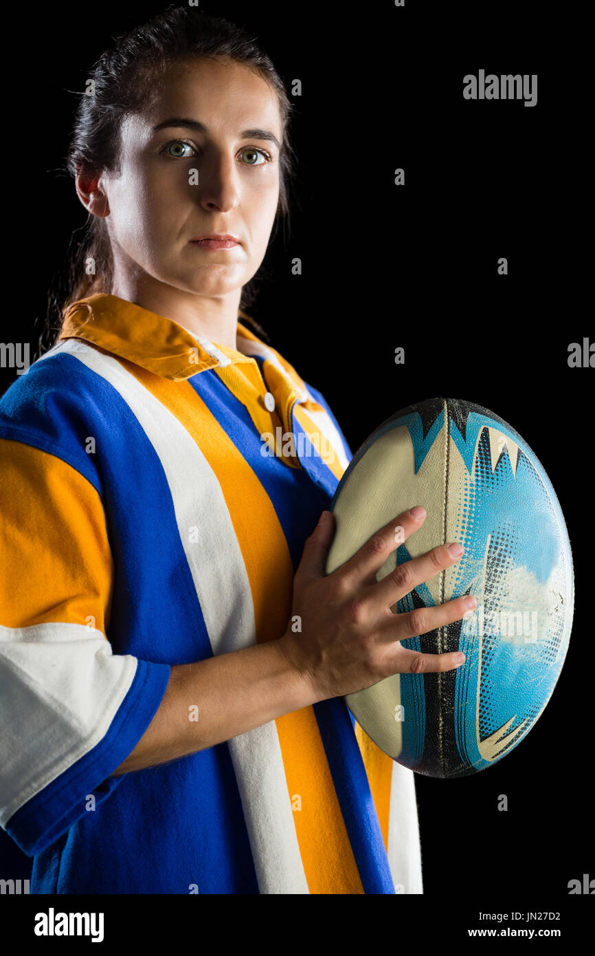 Portrait of confident female rugby player standing against black ...