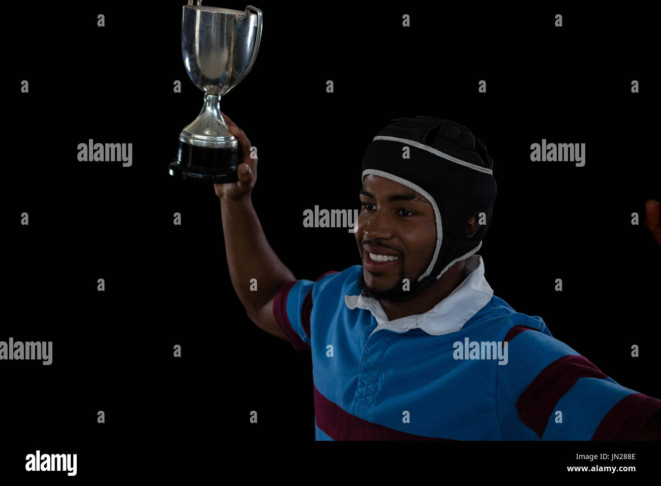 High angle view of happy rugby player holding trophy against black ...