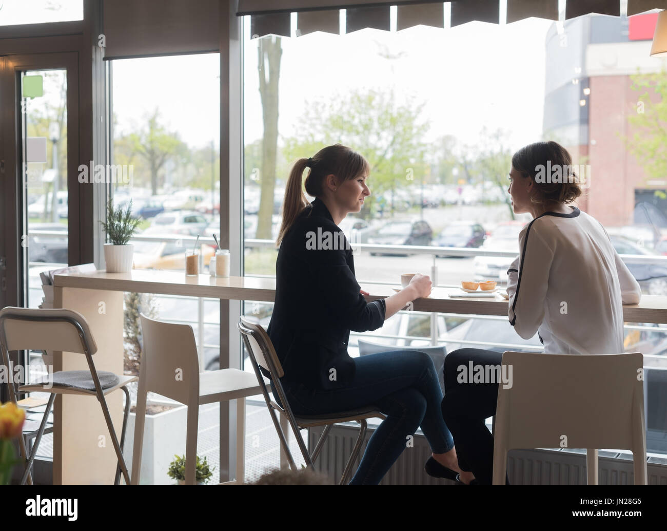 Female friends sitting by window in cafe Stock Photo - Alamy