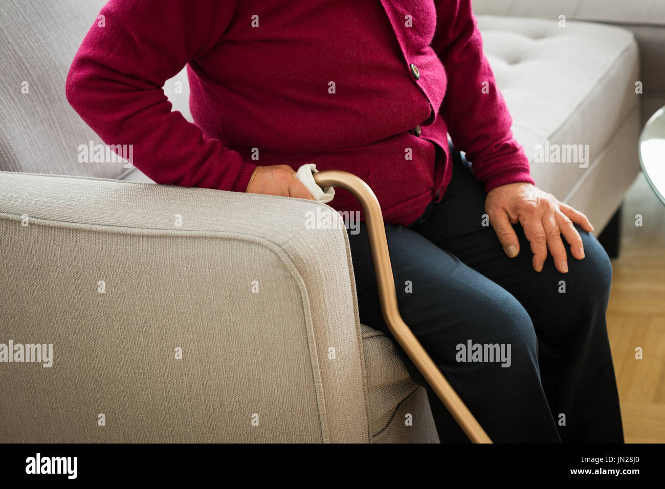Mid section of senior woman holding walking cane while sitting on sofa ...