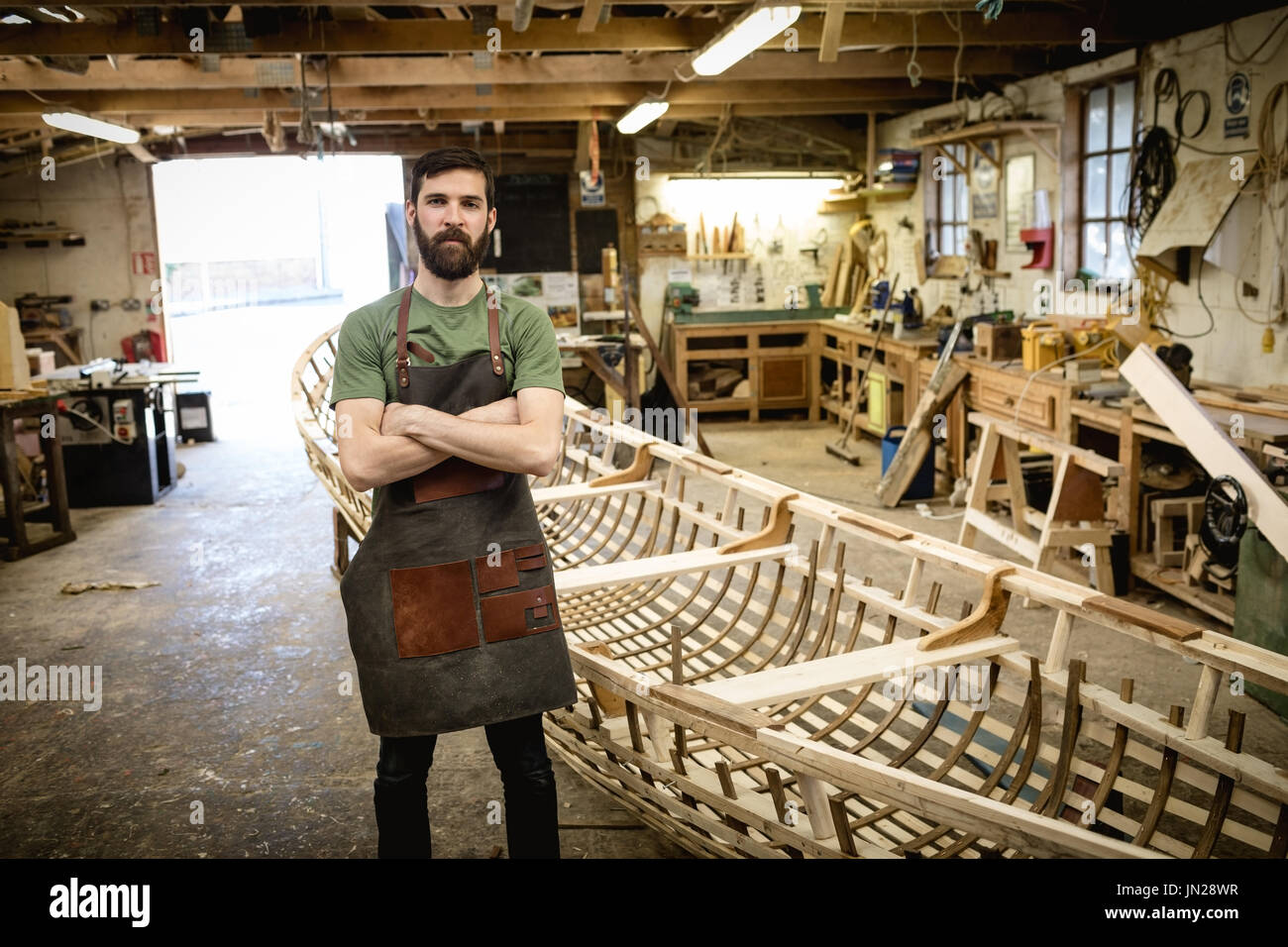 Portrait of confident carpenter standing with arms crossed in workshop ...