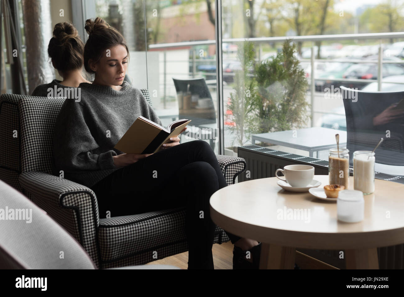 Young woman reading book while sitting on armchair in cafe Stock Photo ...