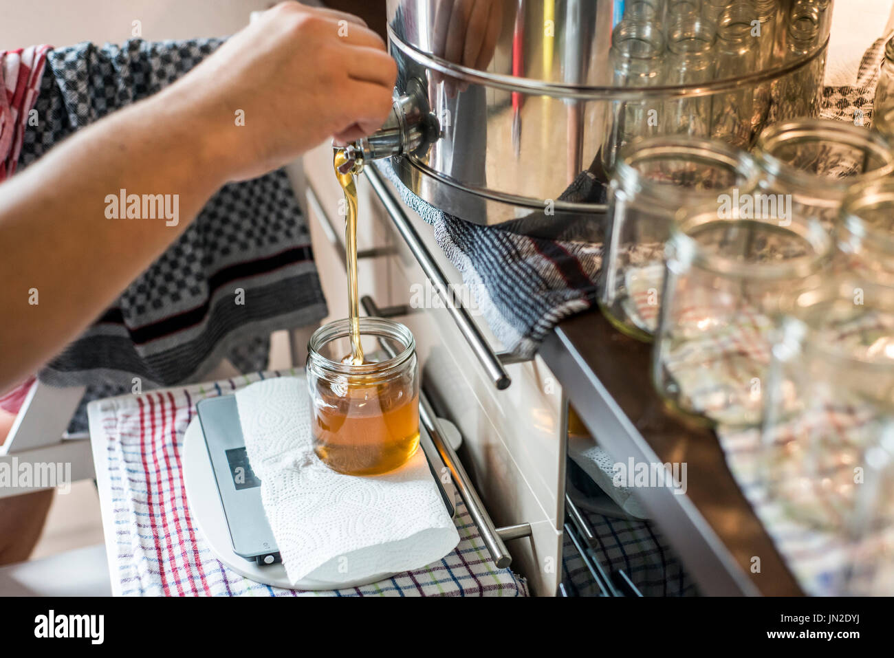 Beekeeper filling up the fresh new honey into glass jars on a scale ...