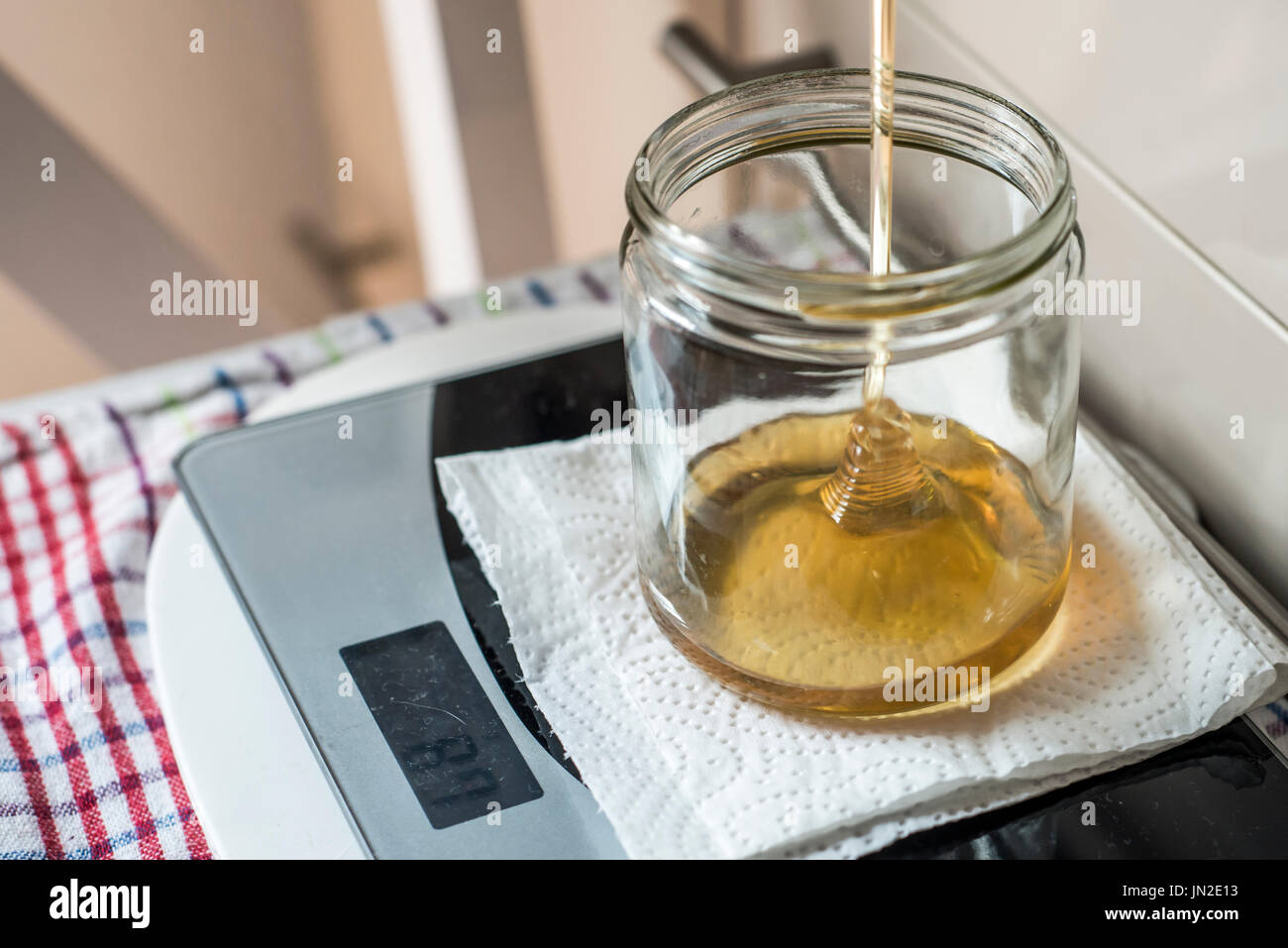 Beekeeper filling up the fresh new honey into glass jars on a scale ...