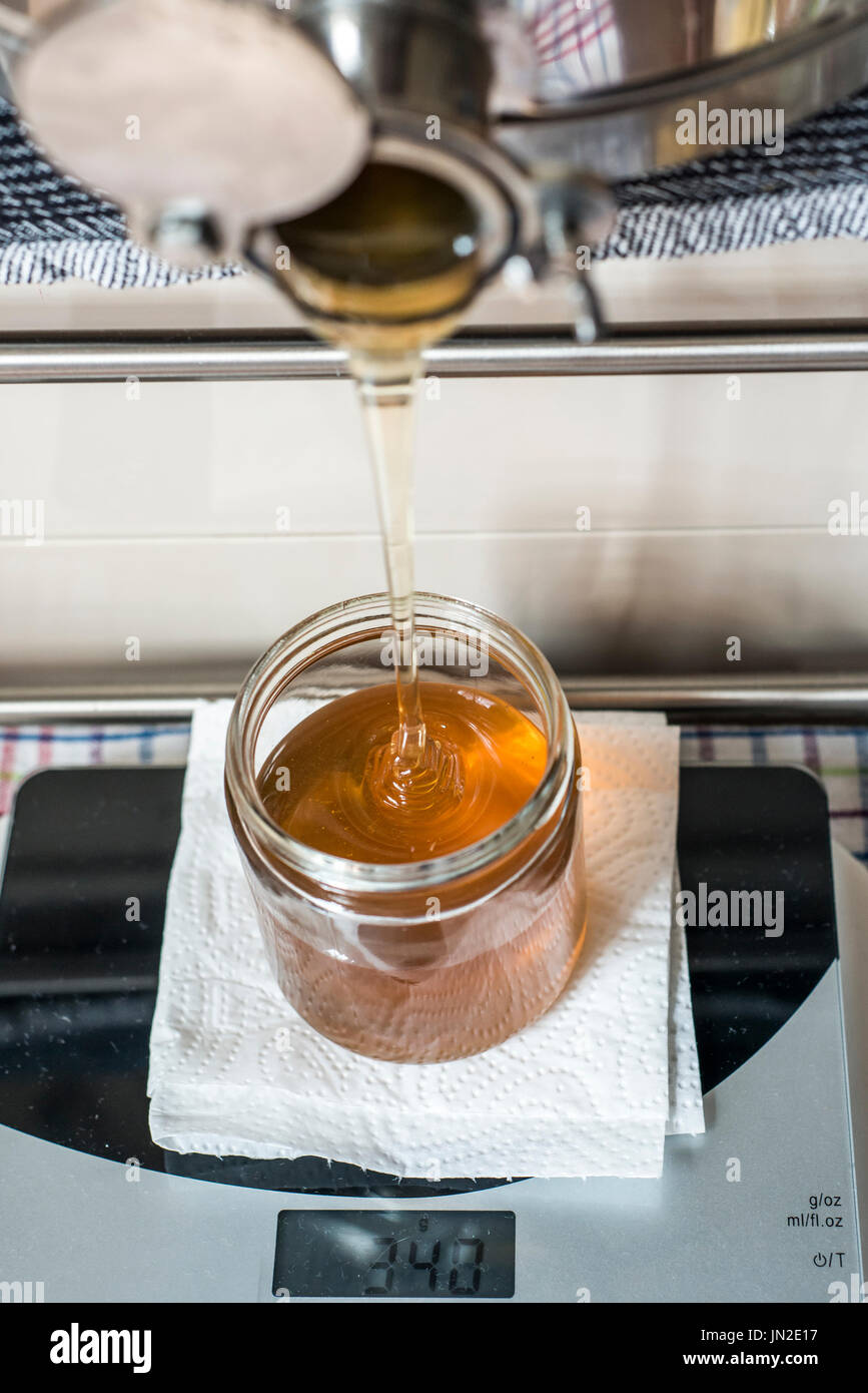Beekeeper filling up the fresh new honey into glass jars on a scale ...