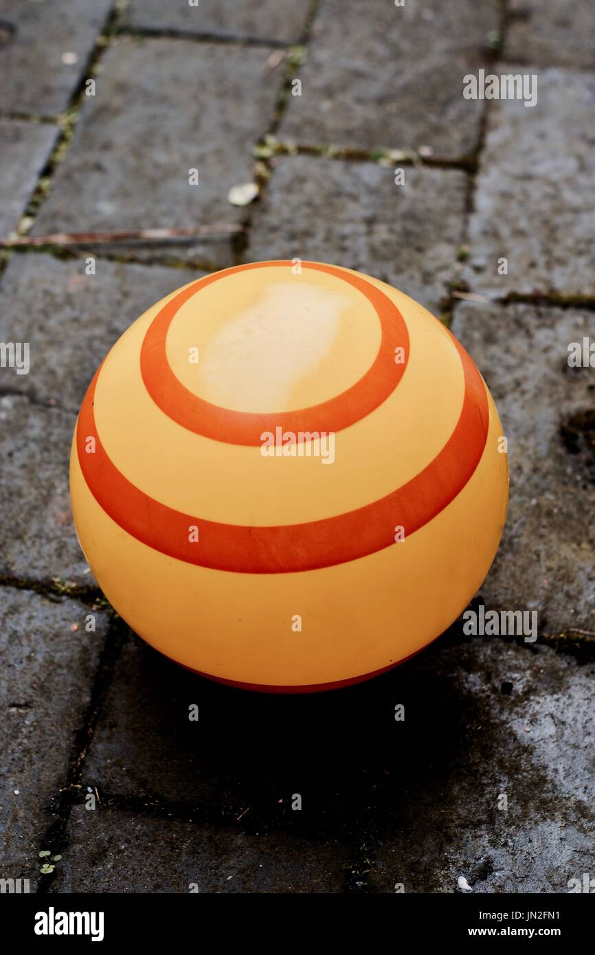 Big yellow ball with red stipes around on the stone floor in garden ...