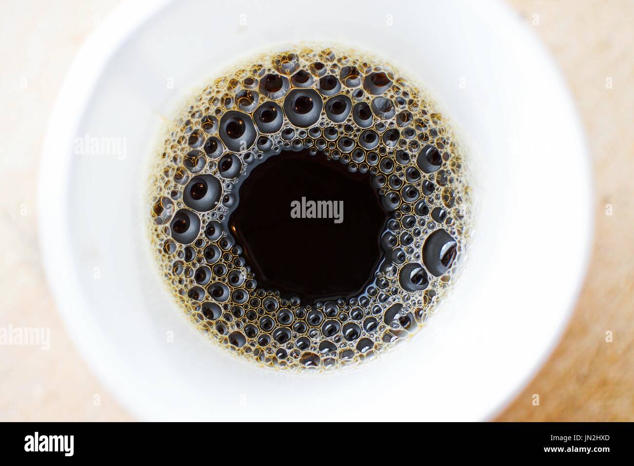 Fresh brewed black coffee bubbling in a white cup on a rustic wood ...