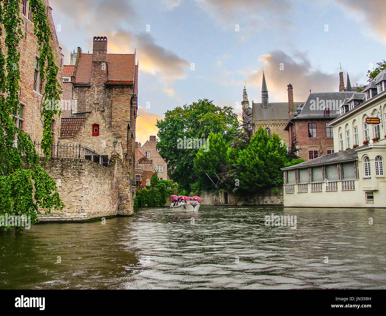 Tourist boat with red umbrellas out glide through the canals of Bruges ...