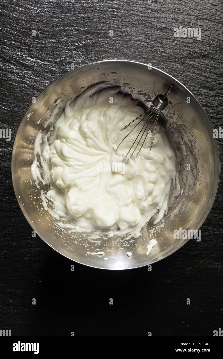 beaten egg whites in a large bowl. bakery products. Cooking. On a black ...