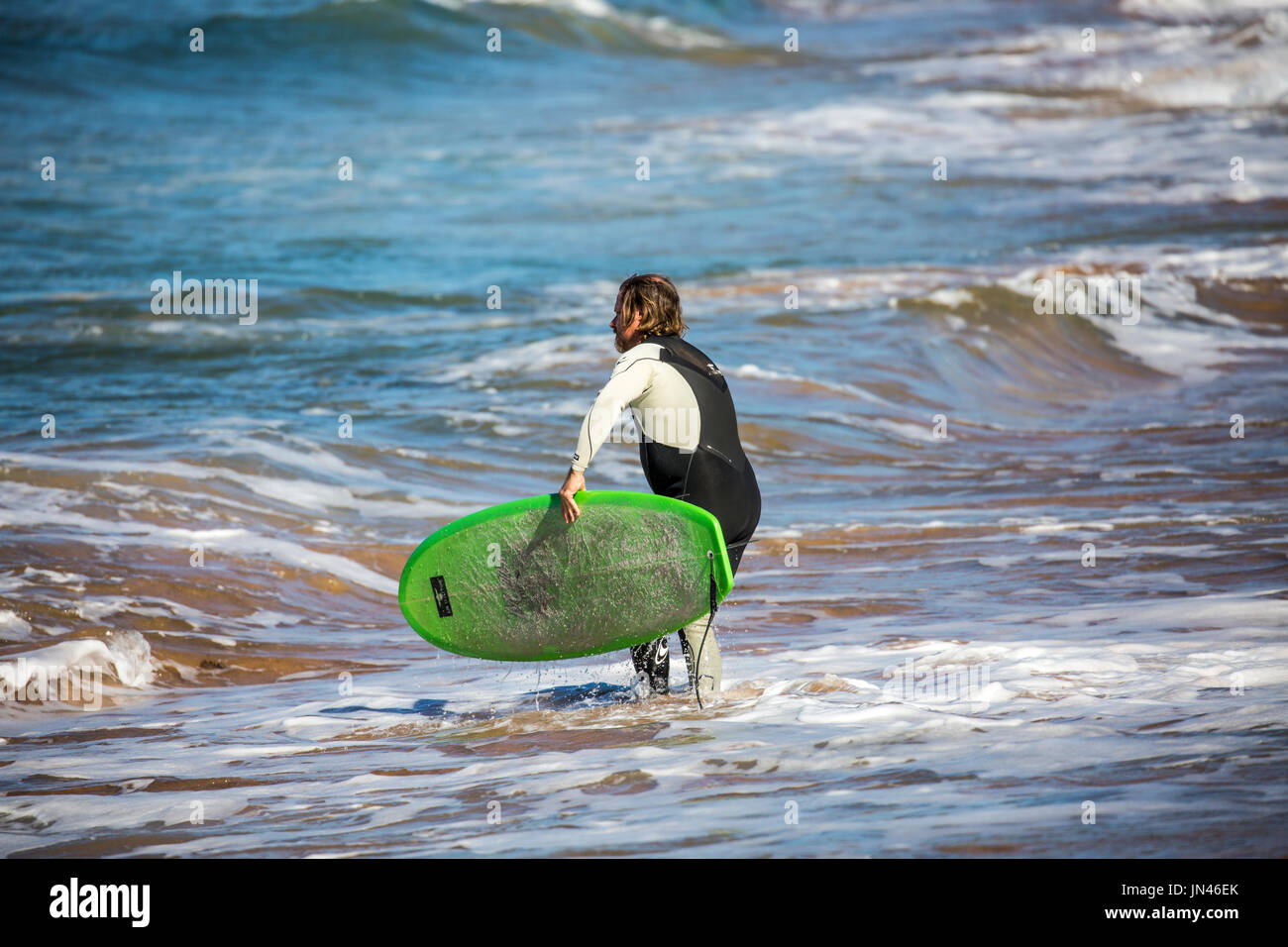 Australian man carrying his surfboard out to sea for surfing at Sydney ...