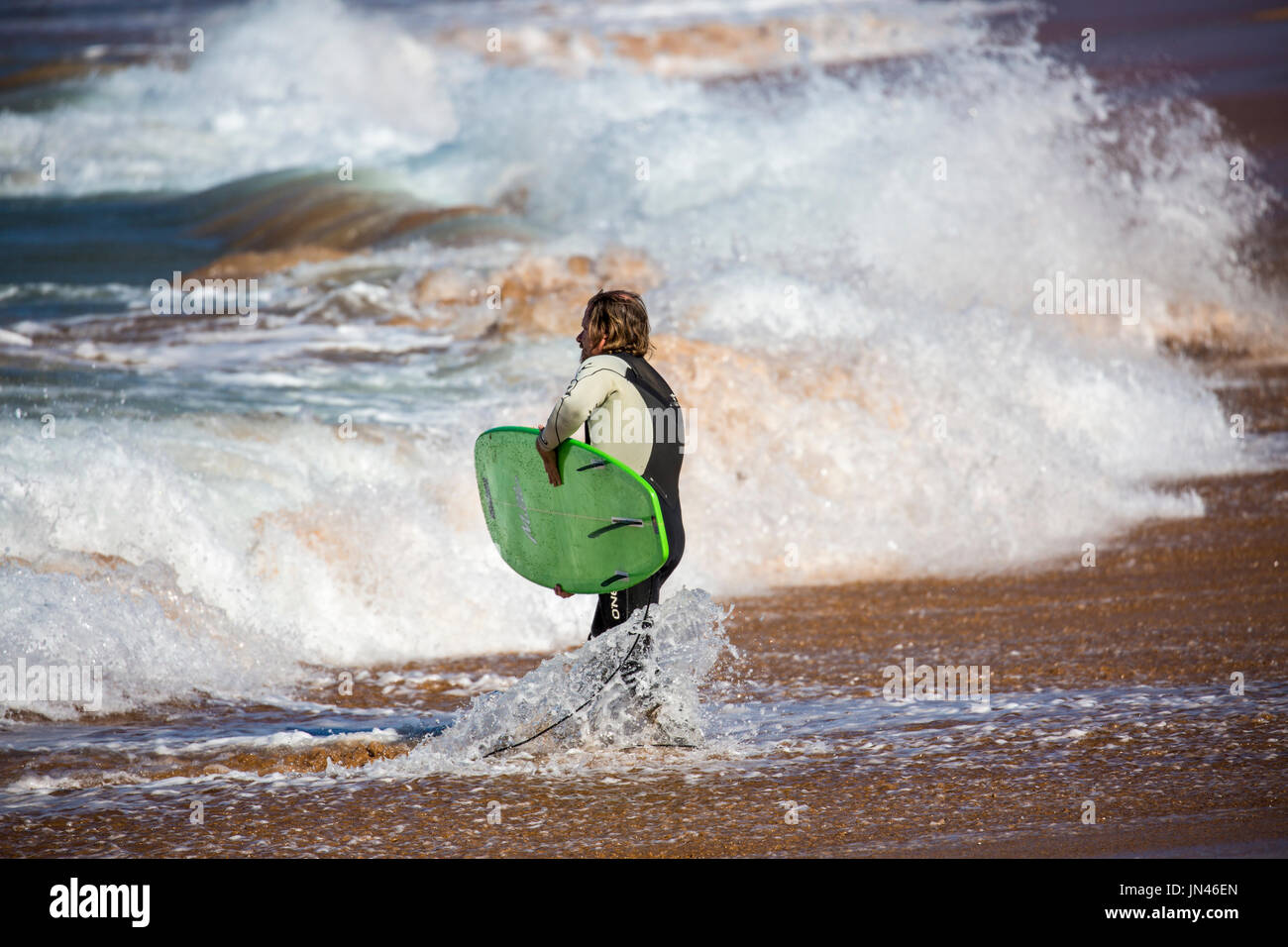 Australian man carrying his surfboard out to sea for surfing at Sydney ...