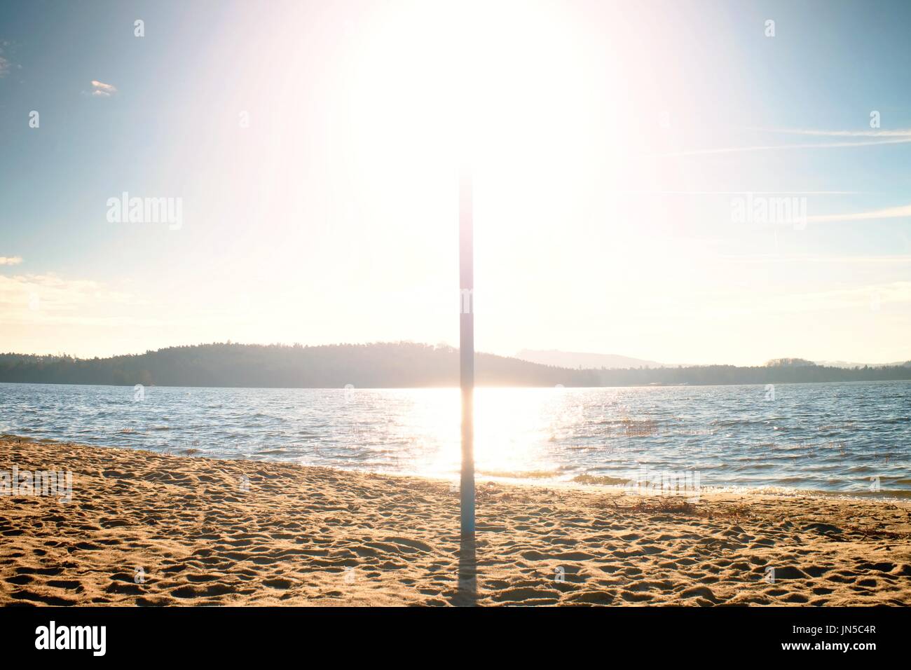 Sun hidden behind blue pole on sandy beach at sea. Forest hill on ...