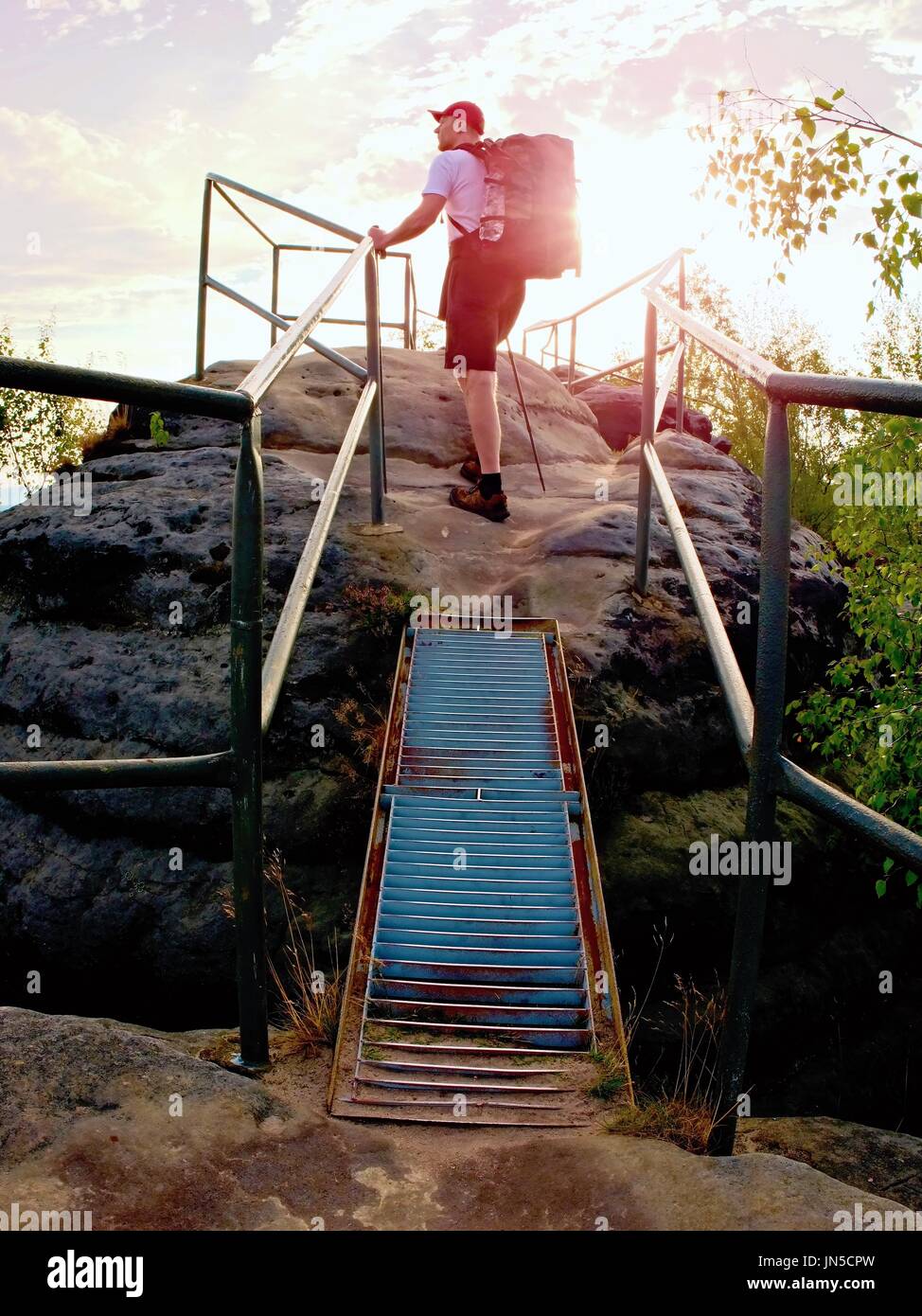 Tired backpacker hold handrail on rock. Sunny spring daybreak in rocky ...