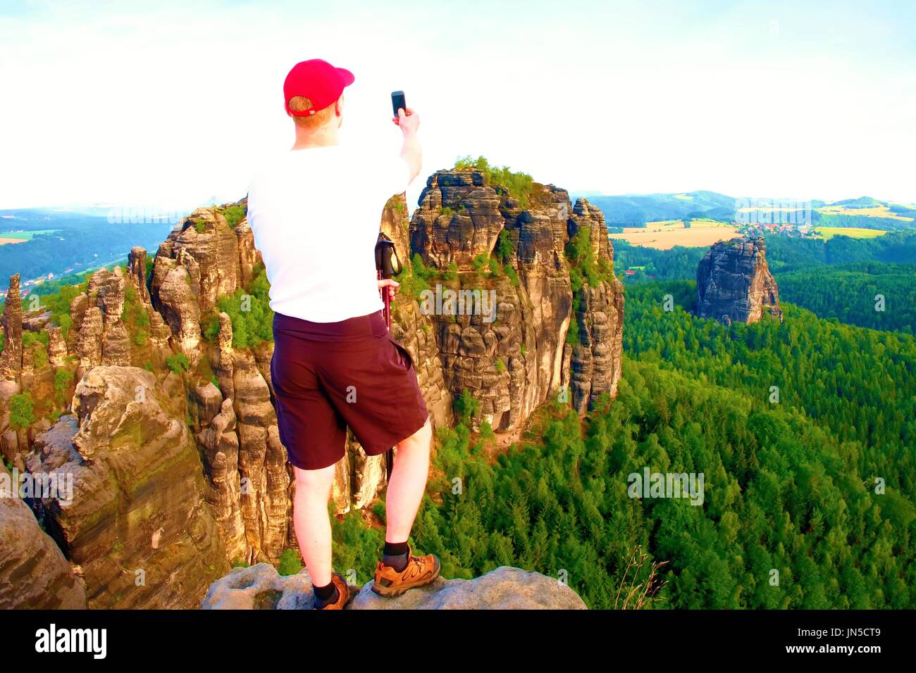 Short hair man on cliff of rock and takes photo by smart phone of ...
