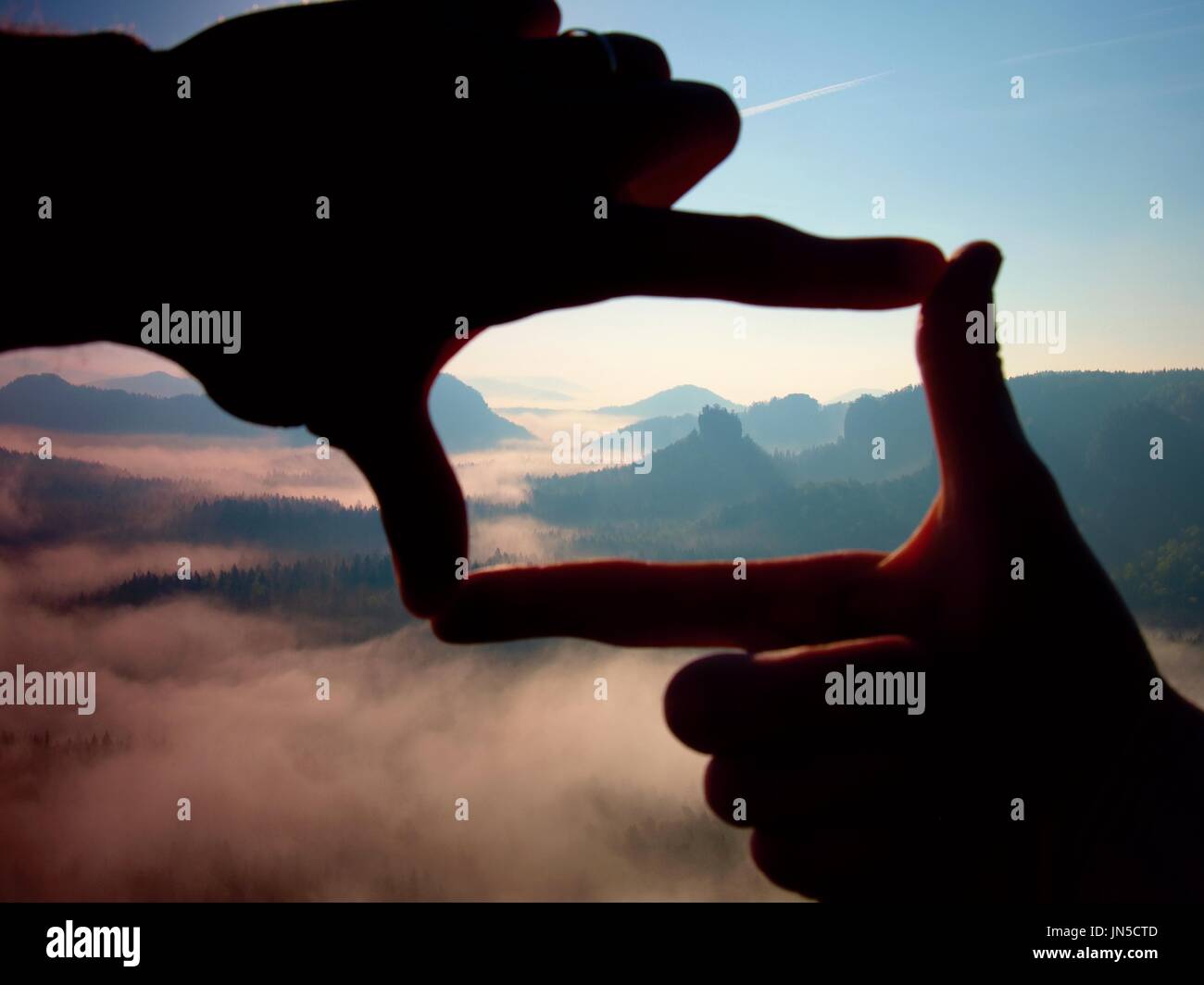 Close up of hands making frame gesture. Blue misty valley bellow rocky ...