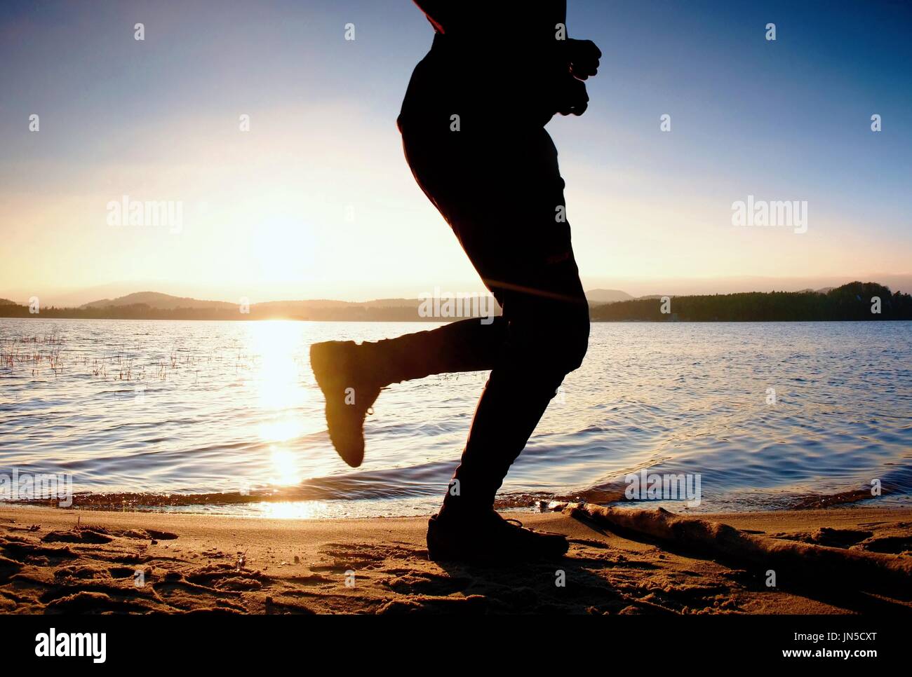 Training at sunset. A silhouette of jogger body at path along lake ...