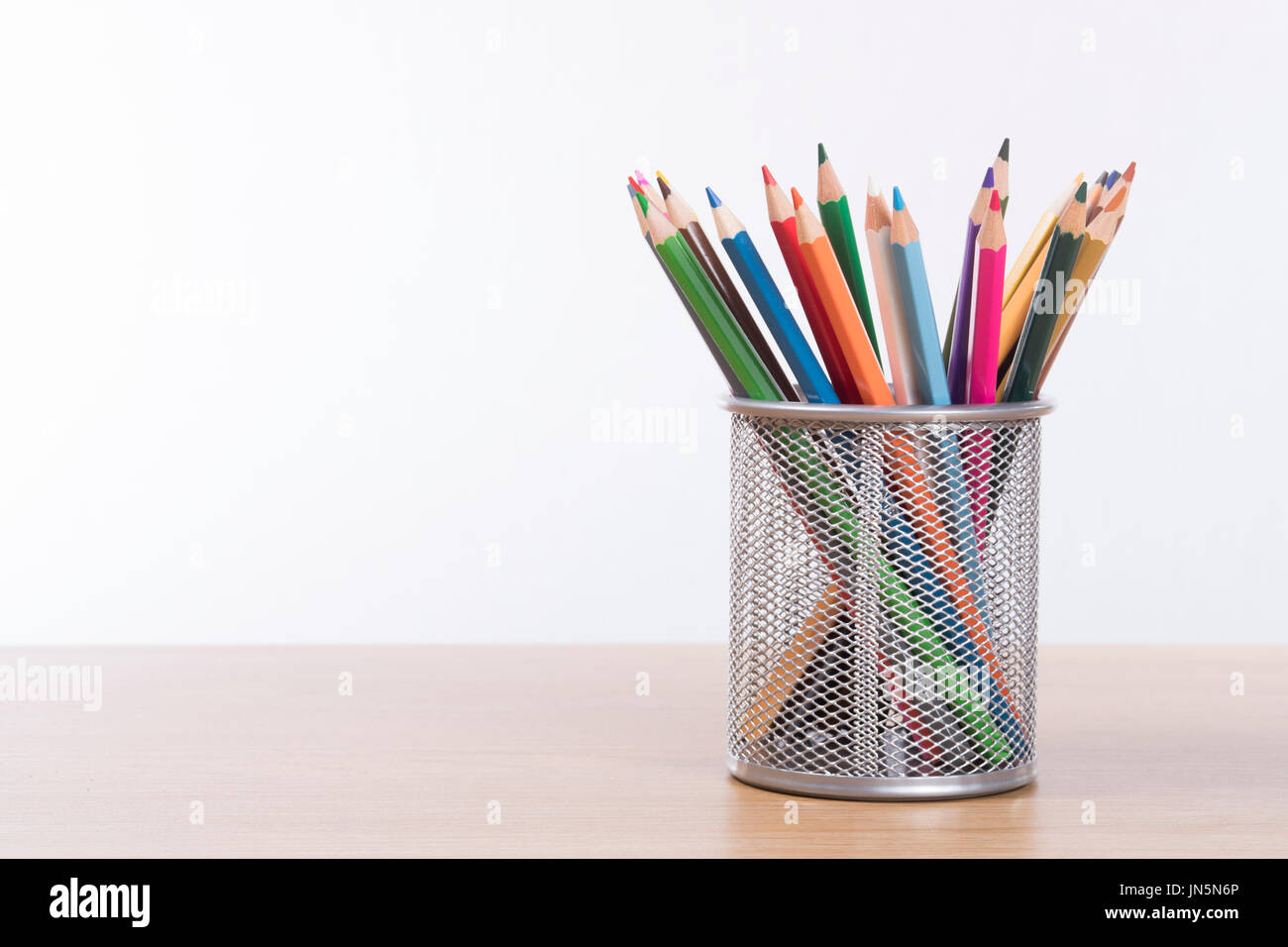 Collection of colored pencil crayons in a wire mesh container on a ...