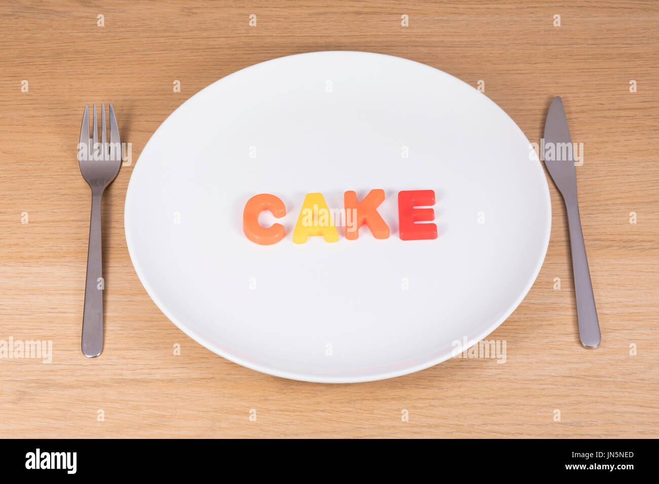 A metal knife, fork and empty white plate with the word cake written in ...