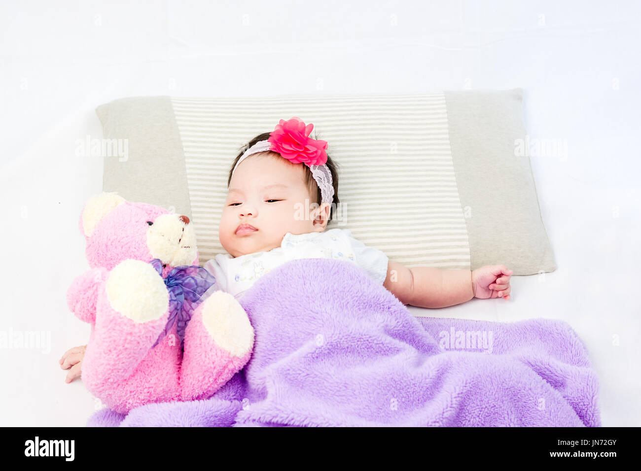 Portrait of sleeping baby lying on a bed with head band and bear doll ...