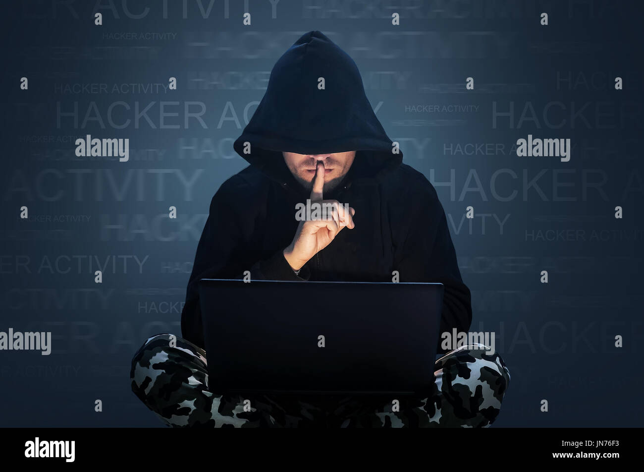 Man with hidden face working at a computer. Holding a finger to his ...