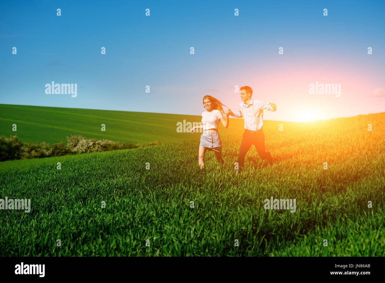 Young happy lovers running on meadow with green grass and blue sky ...