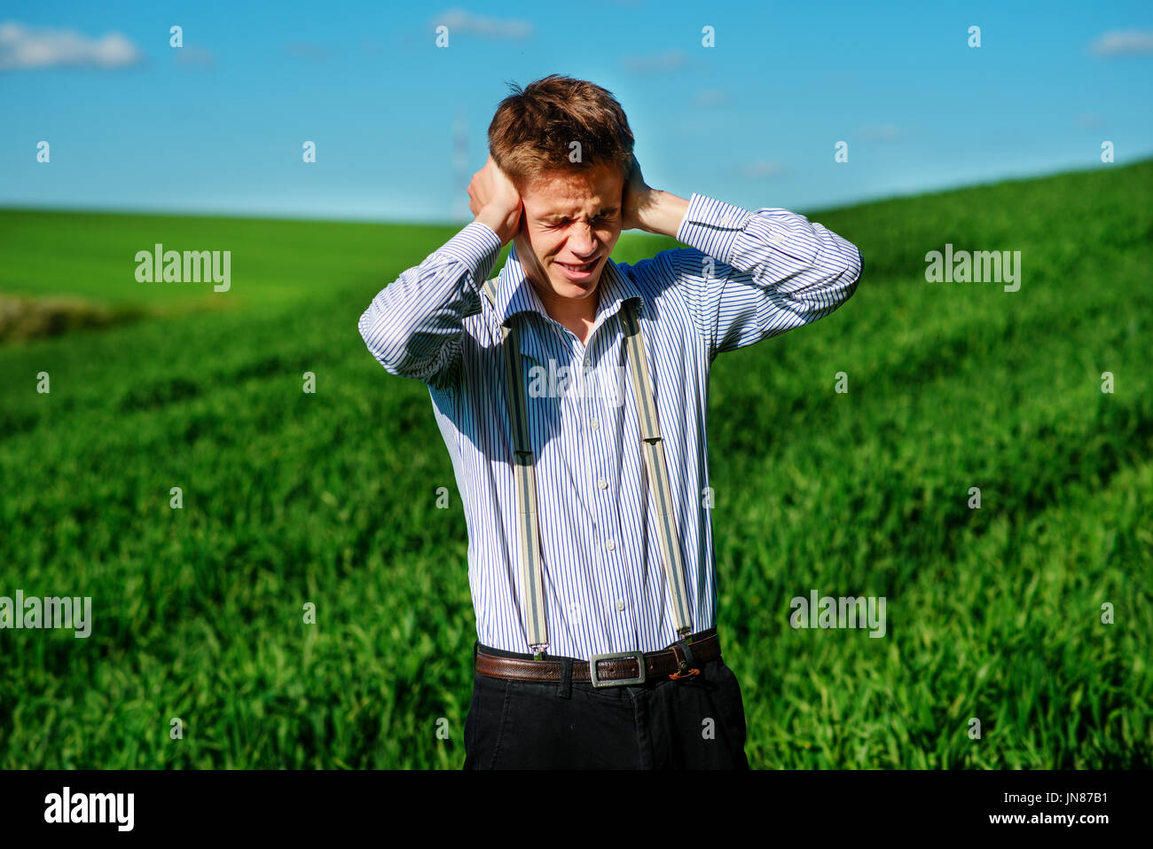 Handsome man in the field is closing his ears with his hands:trying to ...