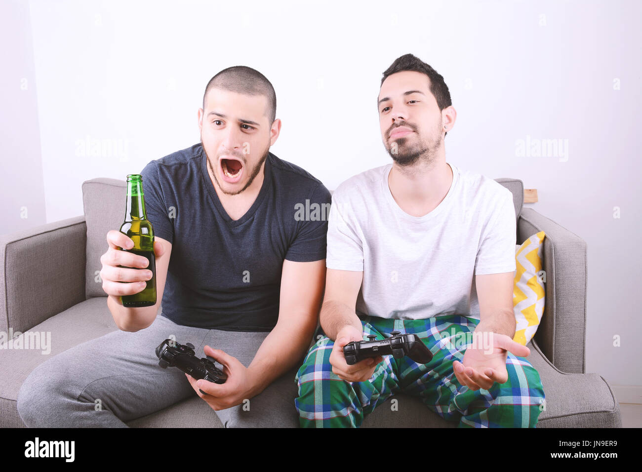 Portrait of two friends playing videogames and sitting on couch ...