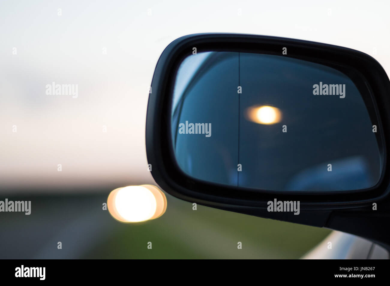 Car lights reflecting in the side mirror of a car parked on the curb of ...