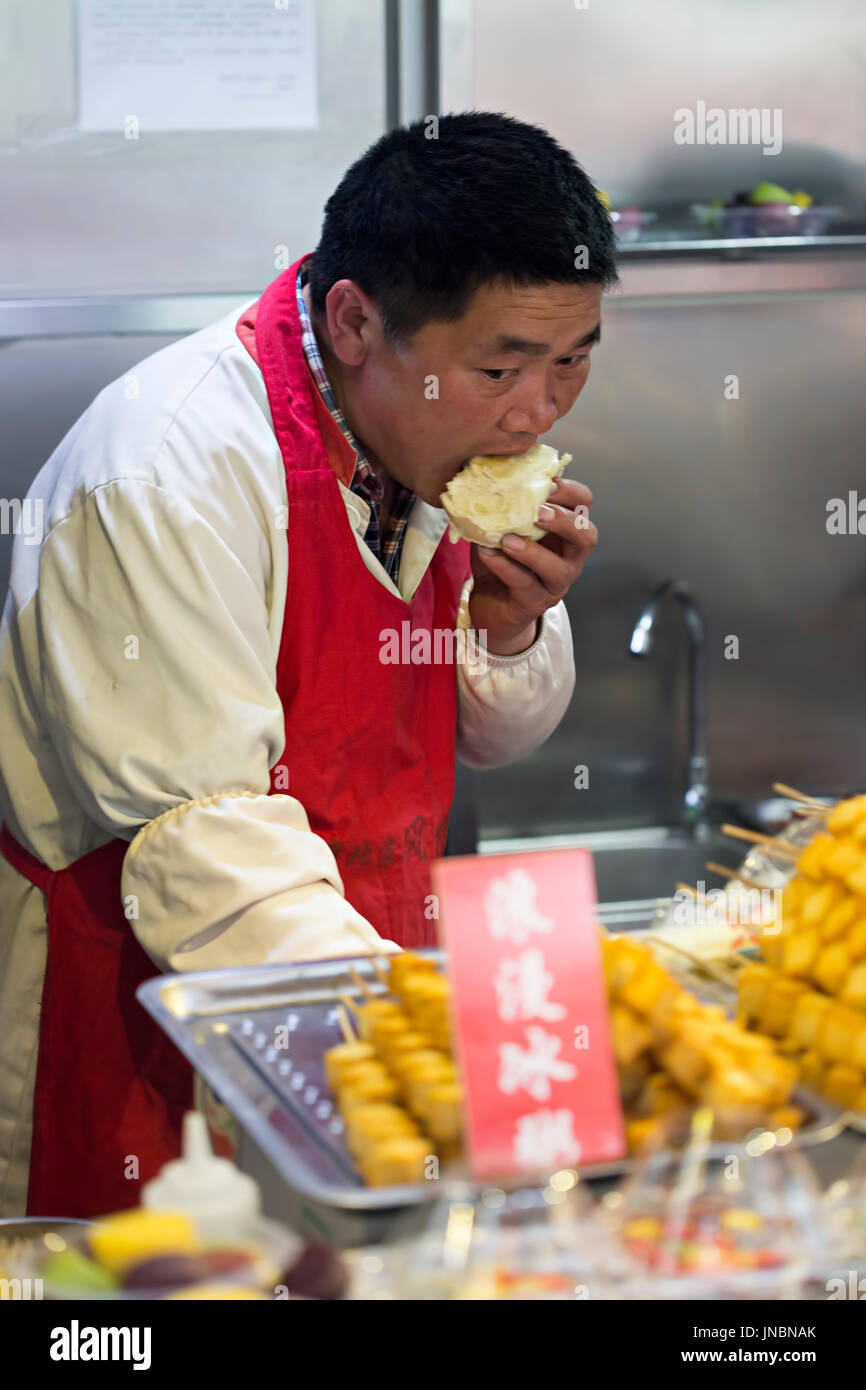 Chinese salesman eating sandwich on traditional food market. Wangfujing ...