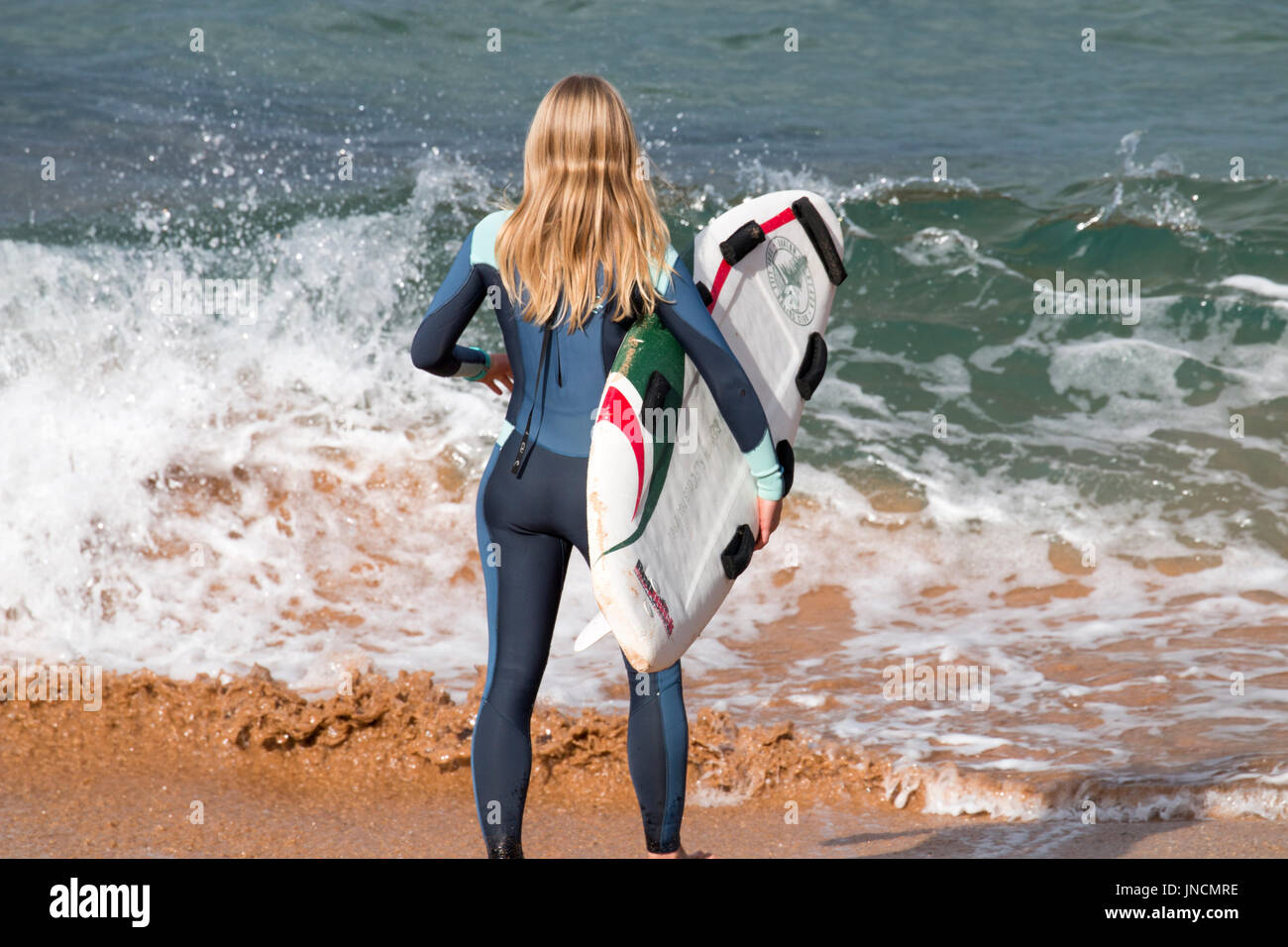 Rear view of blonde australian girl stood on a beach holding her Stock ...