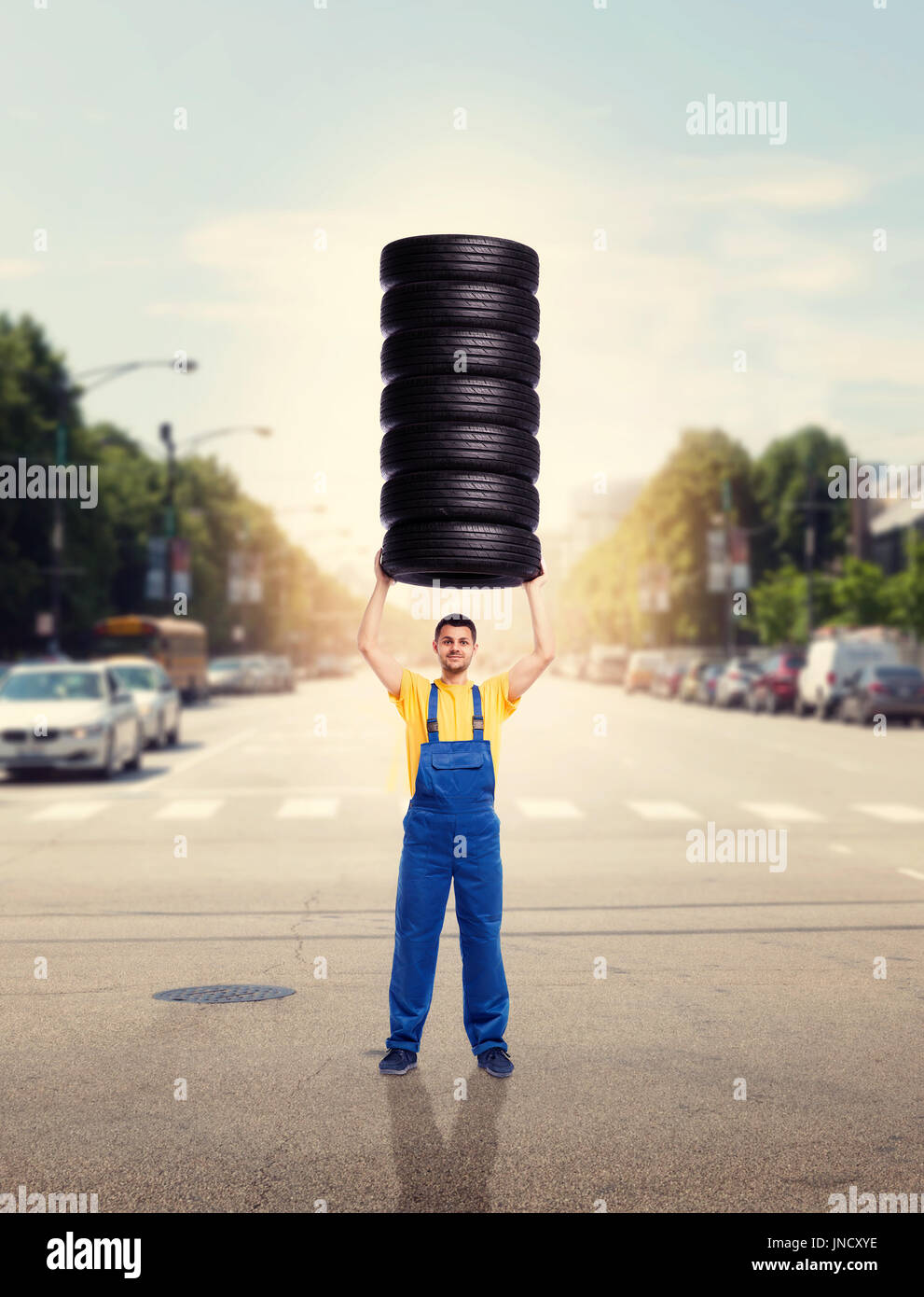 Tyre service worker in uniform holds pile of tires over head. Repairman ...