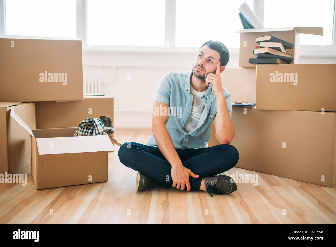 Thoughtful man sitting in yoga pose among cardboard boxes, housewarming ...