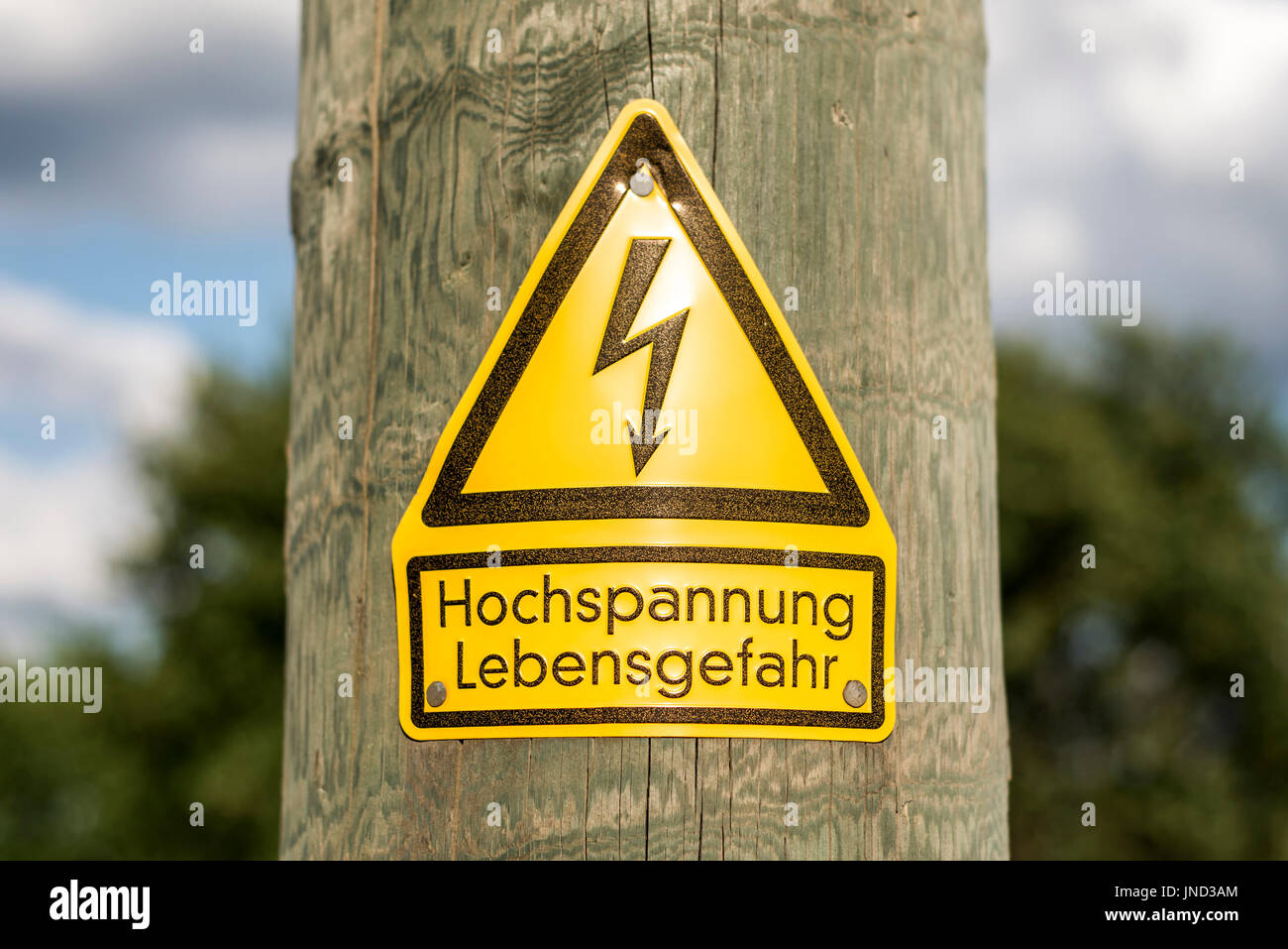 German high voltage sign mounted on wooden pole with green tree in the ...