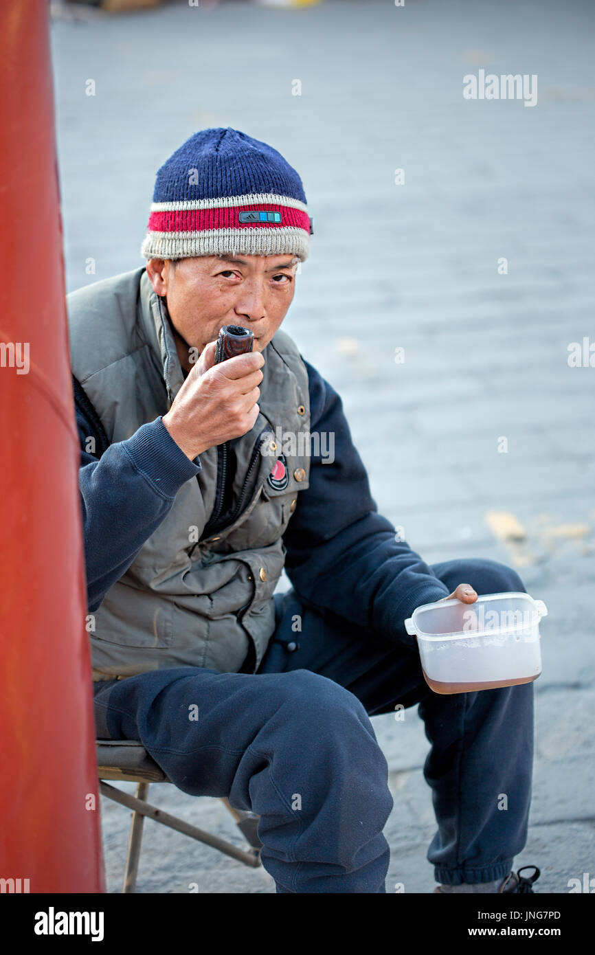 Chinese salesman on flea market smoking pipe Stock Photo - Alamy