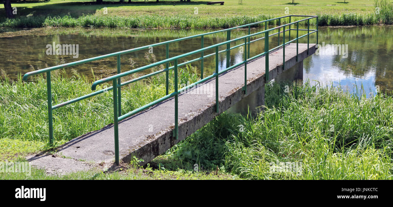 A narrow old aged concrete bridge on the city public pond. The water ...