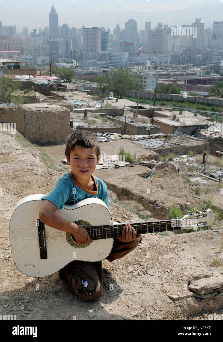 URUMQI, China - A boy holds a guitar on a rooftop overlooking a slum ...