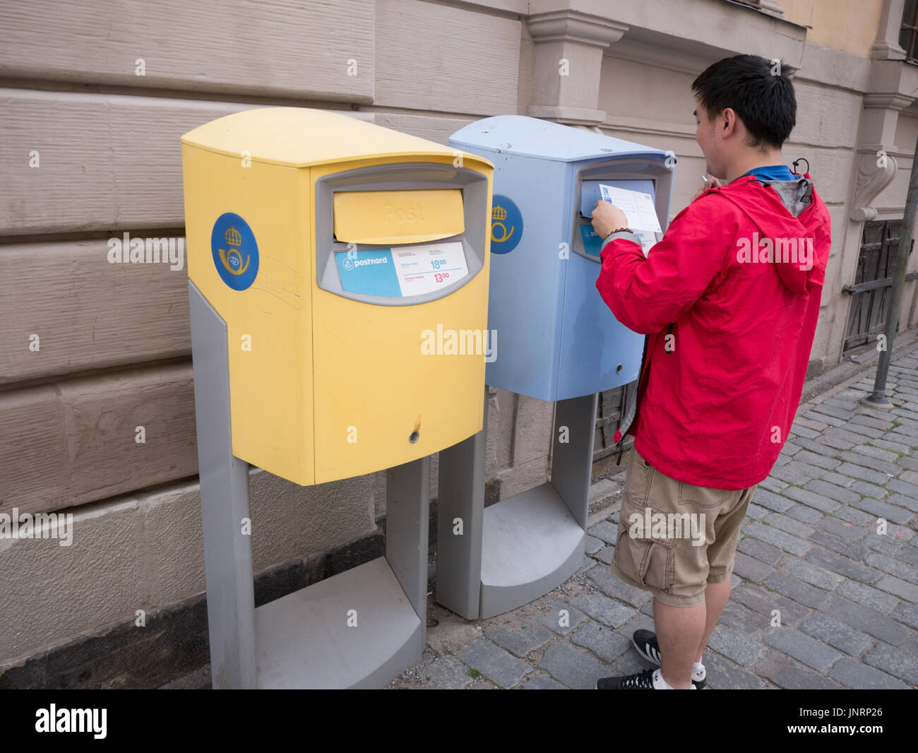 Tourist posting postcard into Postnord Swedish post postbox Stockholm ...