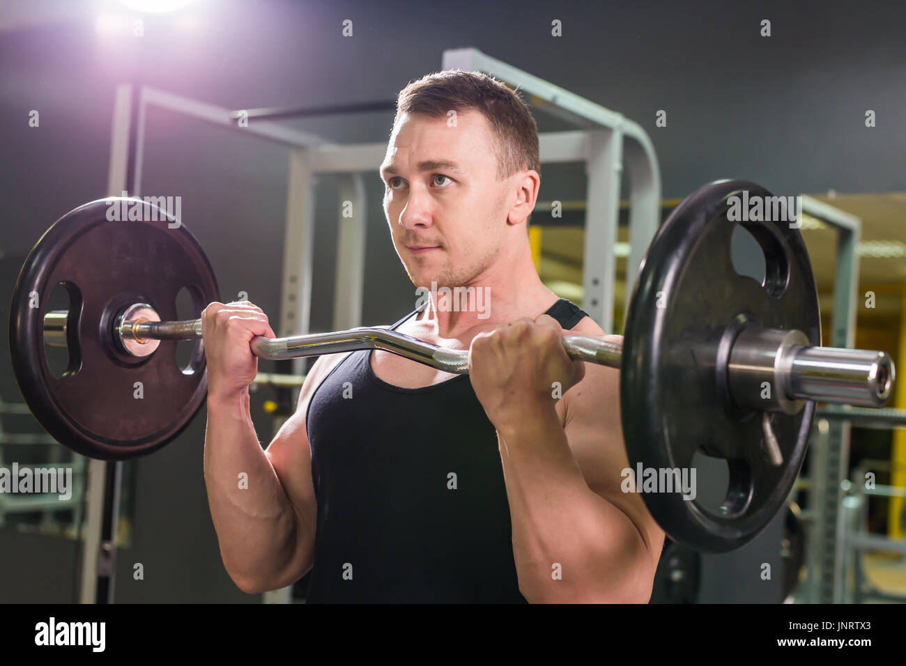 Muscular man with pulling up barbell in fitness training class indoors ...