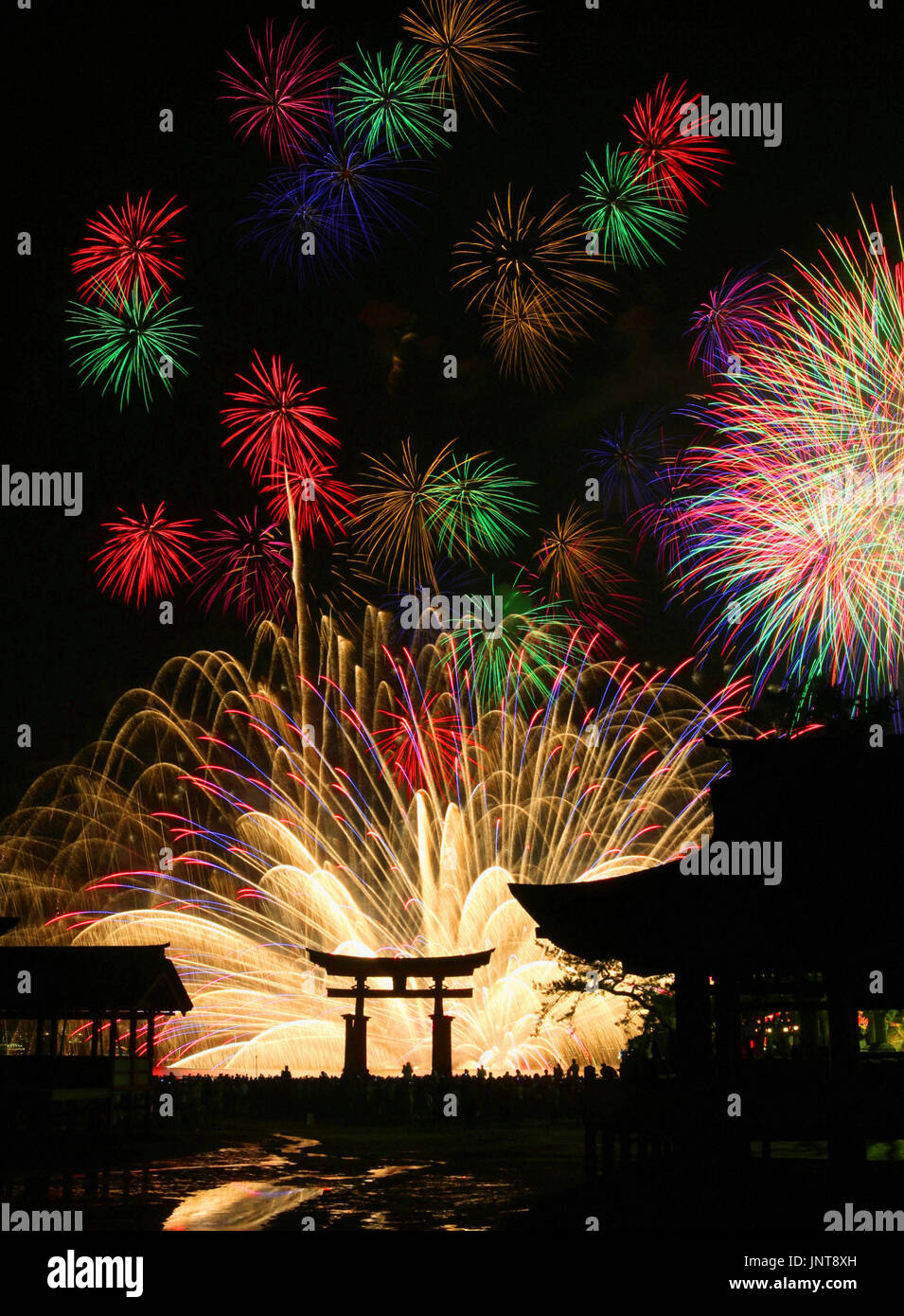 HIROSHIMA, Japan - Fireworks light up a torii gate and buildings in an ...