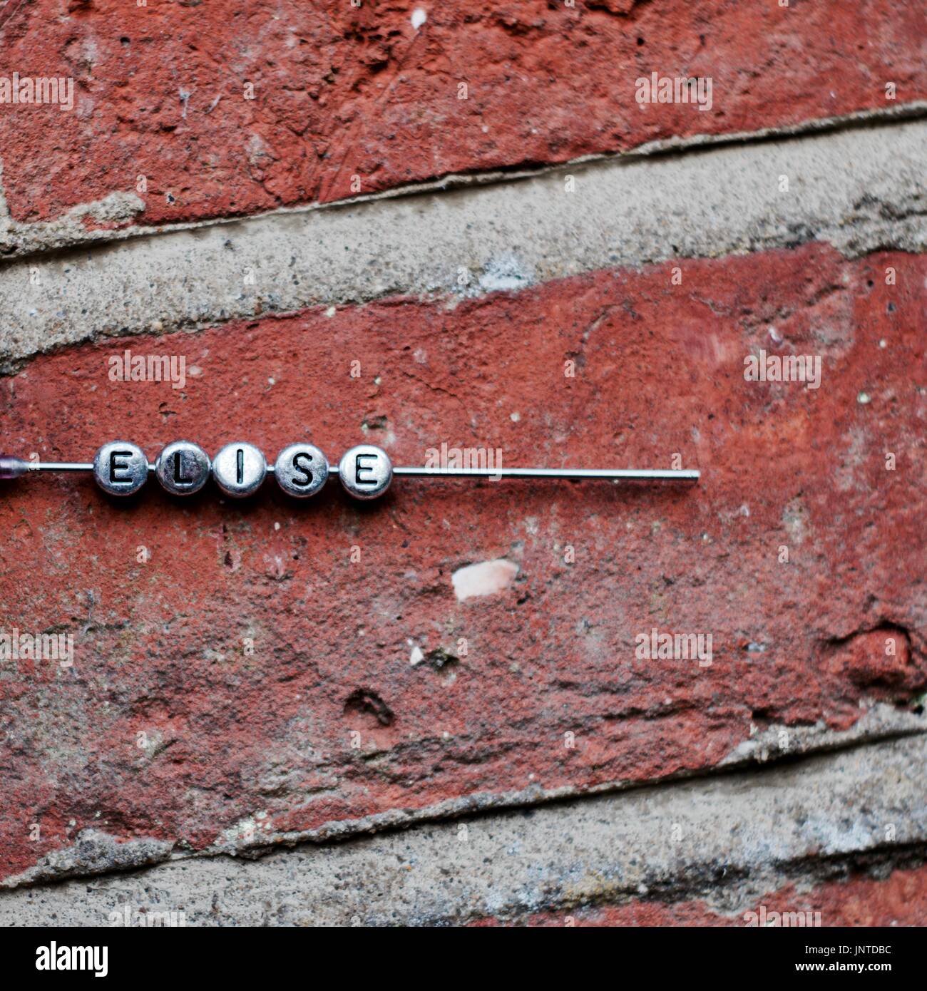 Small silver pins letters Elise on the needle. Brown brick dirty ...