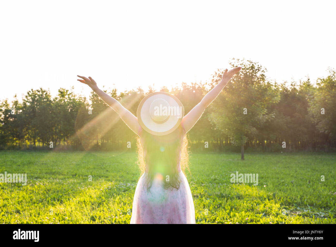 Free happy young woman raising arms watching the sun in the background ...