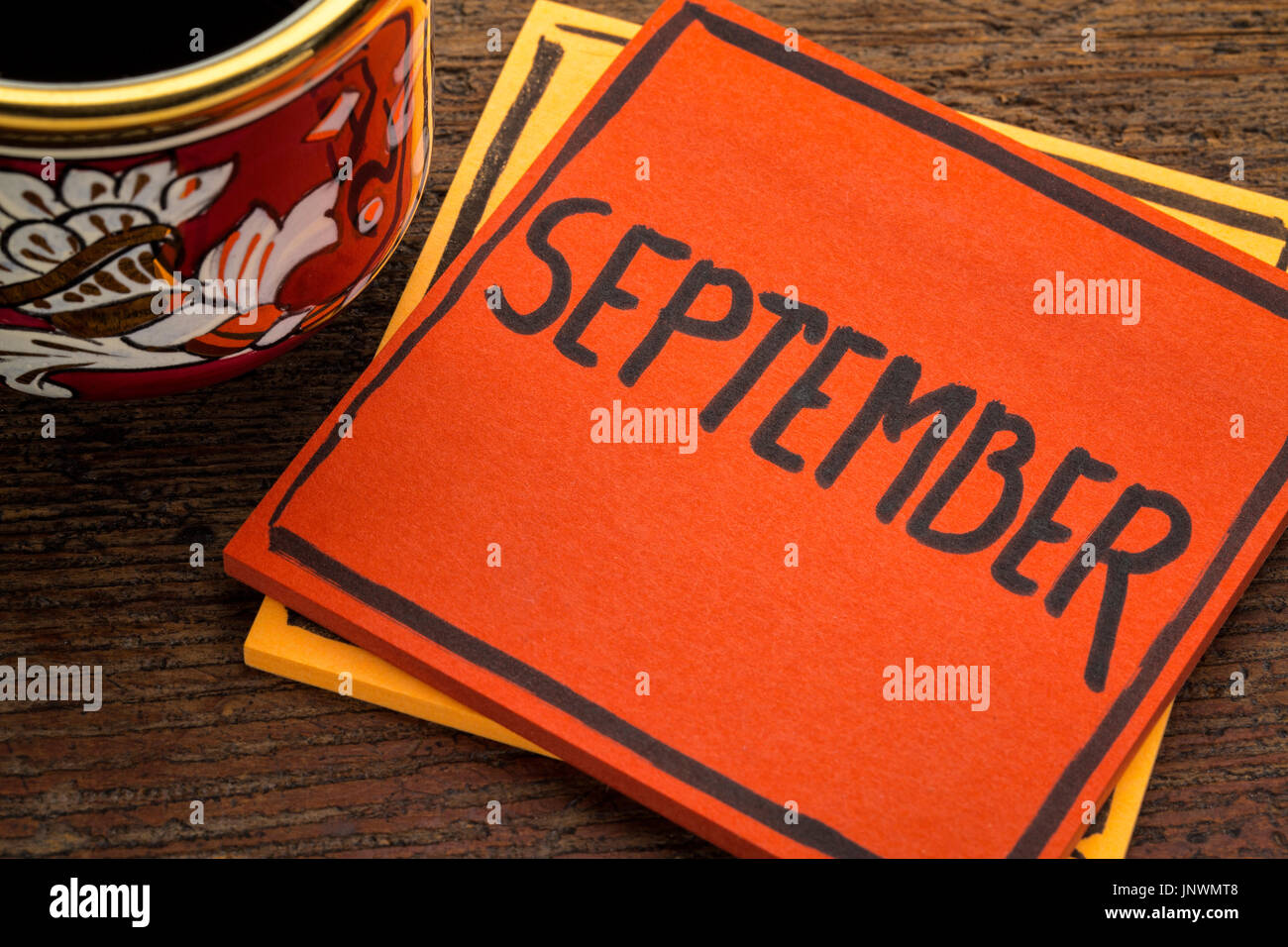 September - handwriting in black ink on a sticky note with a cup of ...