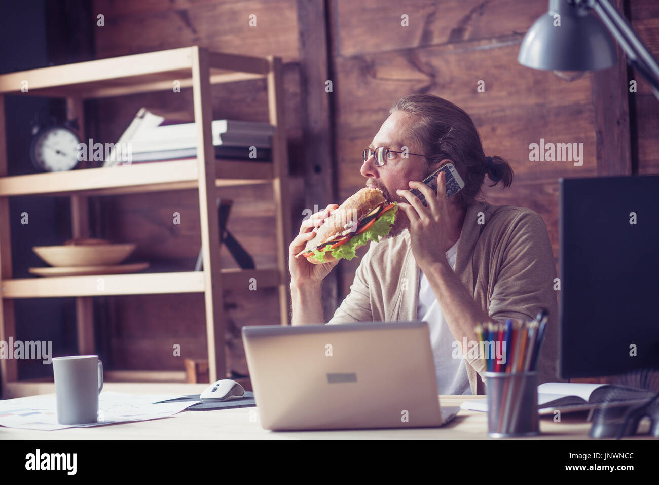 Freelancer eating sandwich while talking on phone Stock Photo - Alamy