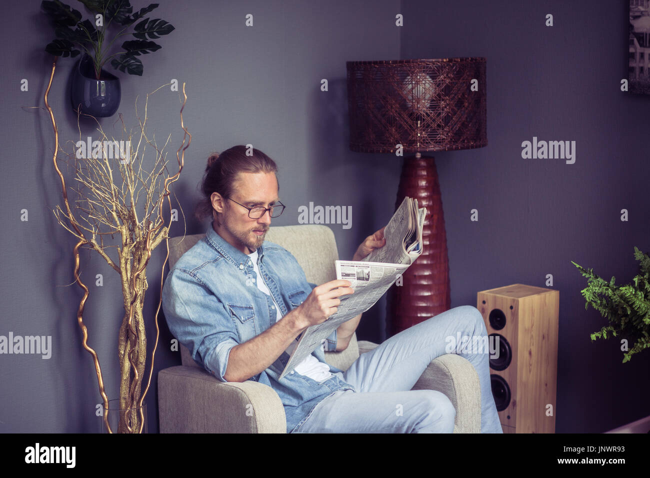 Young man sitting in chair reading newspaper Stock Photo - Alamy