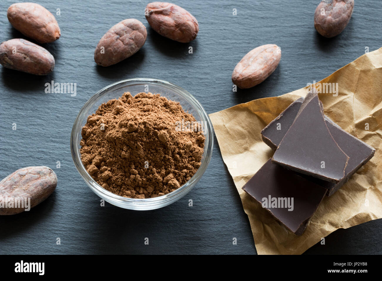 Raw cocoa powder, raw cacao nibs and several pieces of chocolate on a ...