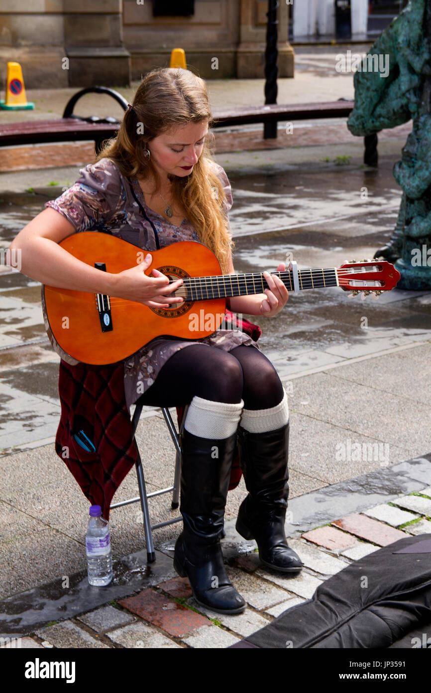 A young Southern Irish female student busker playing a guitar and ...