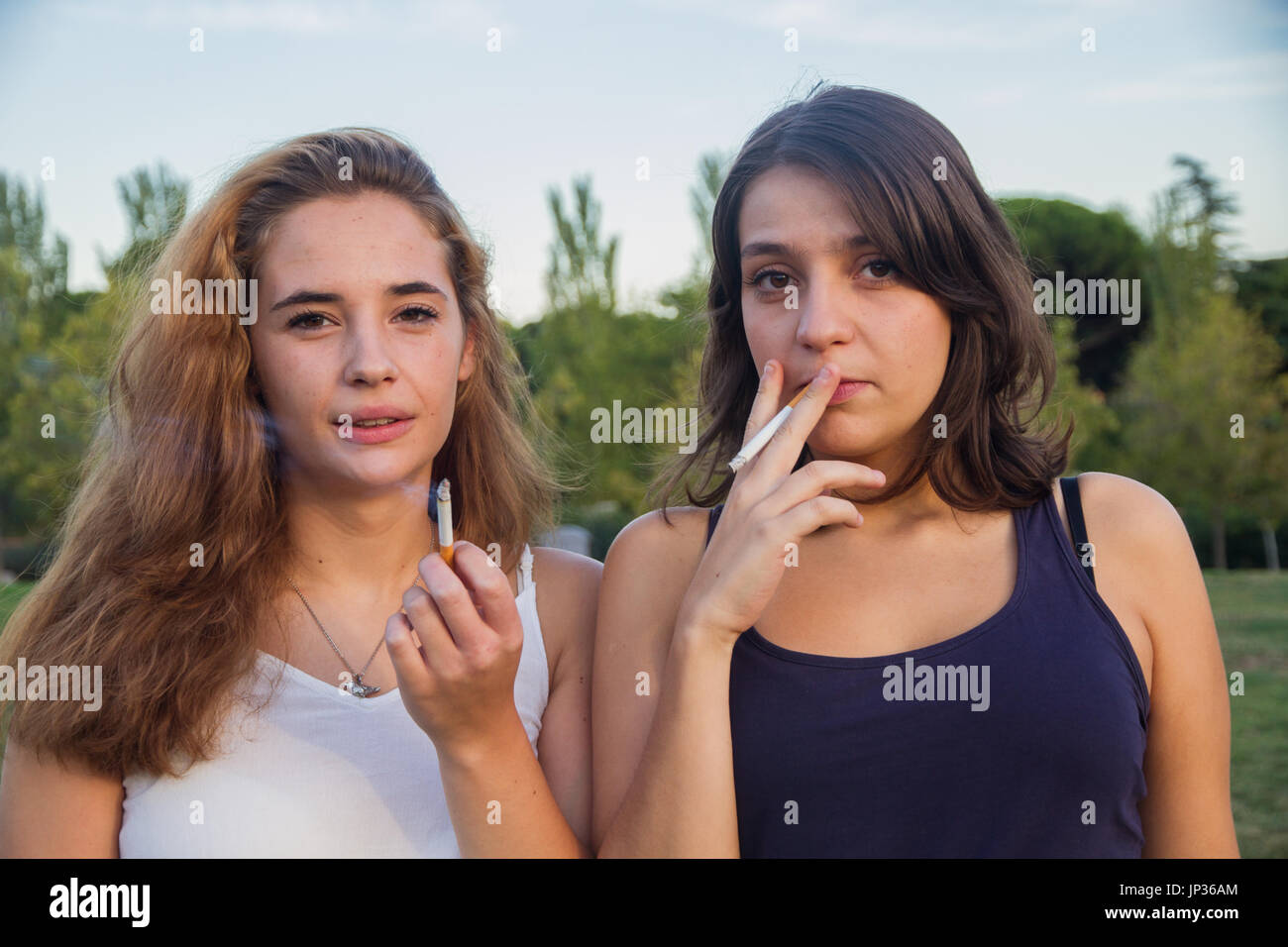 Two girls friends smoking cigarettes in the park on a cloudy day. They ...