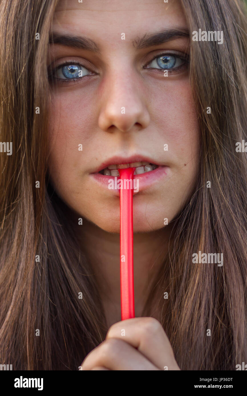 Young girl with blue eyes and brown hair eating red licorice. Portrait ...