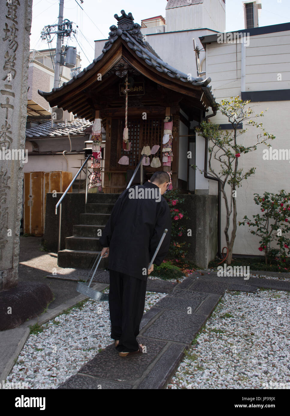 A female Buddhist monk dressed in black sweeping a stone pathway at the ...