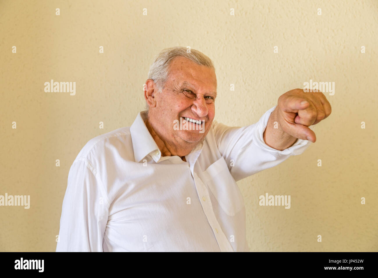 Handsome old man in white shirt is pointing away, looking at camera and ...